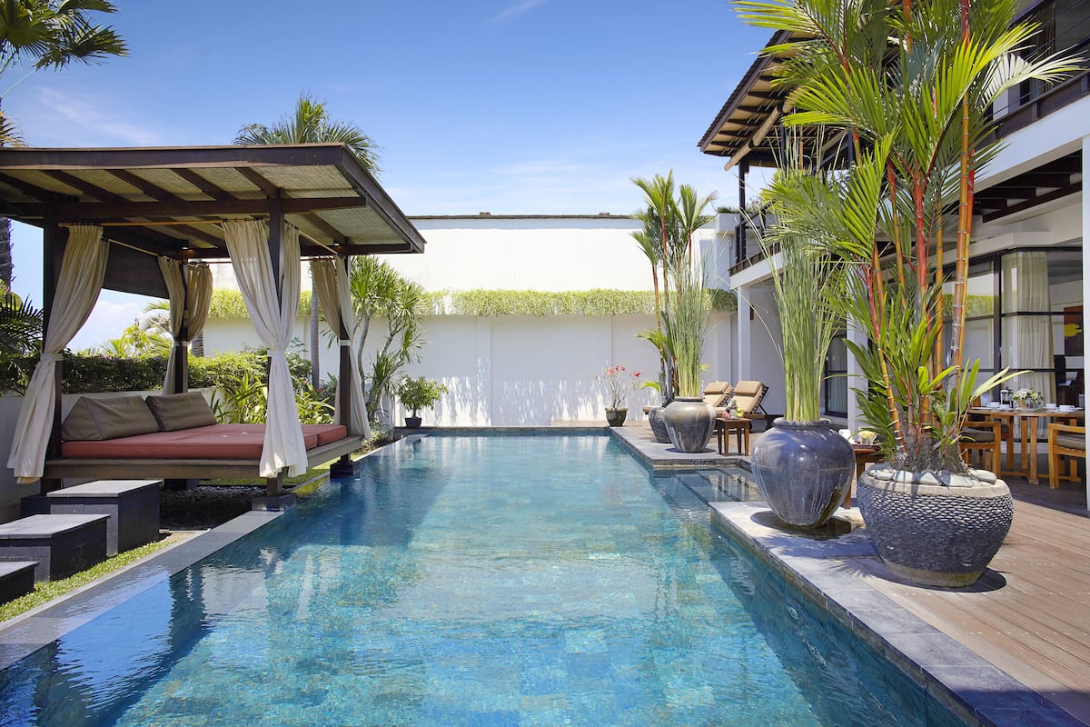 Piscina com área de estar coberta, plantas em vasos e deck de madeira.