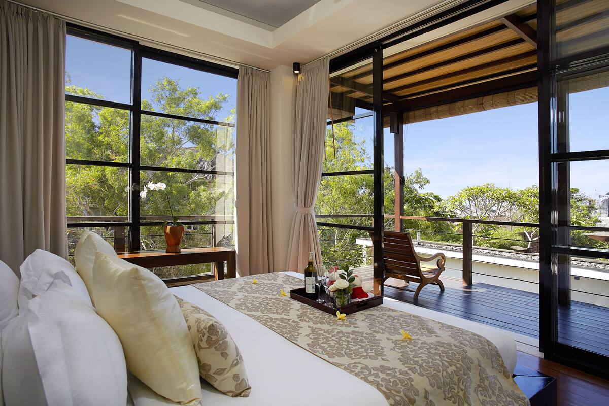 Quarto espaçoso com uma cama grande, teto de madeira e varanda com vista para árvores.