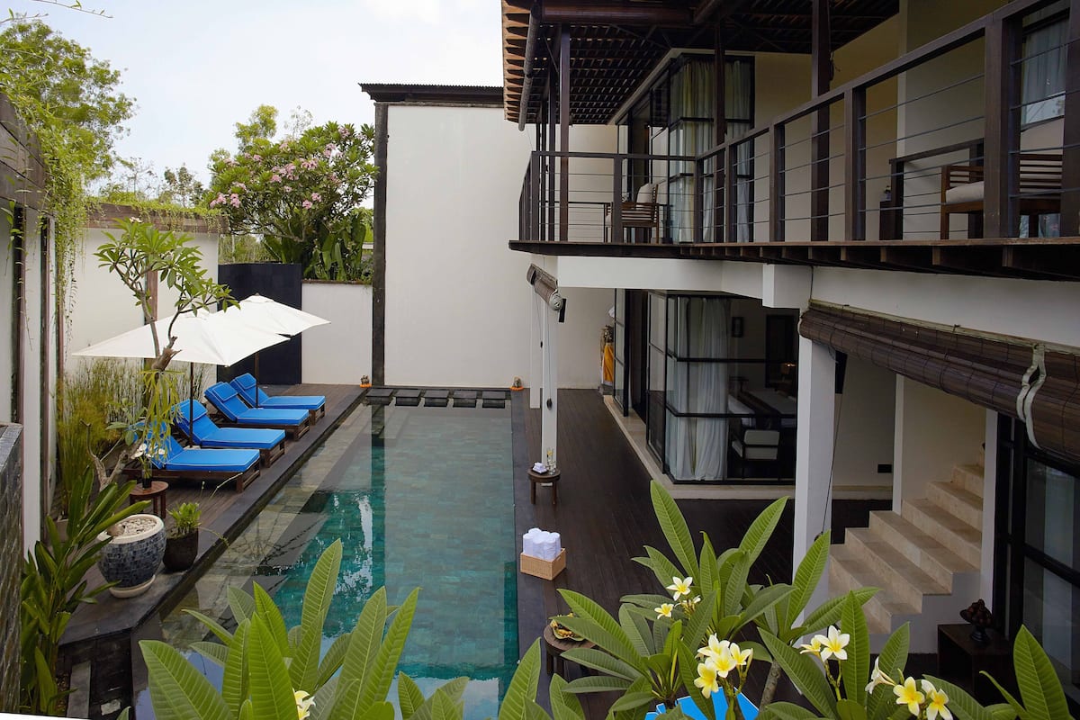 Uma casa moderna com piscina, cadeiras de descanso azuis e uma varanda com vista para a piscina.