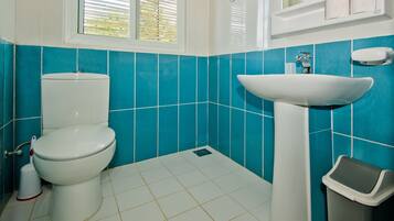 Casa de banho com sanita, lavatório e um contentor de lixo, com azulejos azuis e brancos.
