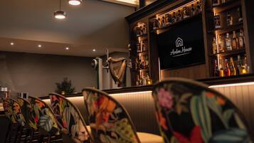 Uma área de bar com um letreiro que diz 'Alden House', banquetas e prateleiras com garrafas.