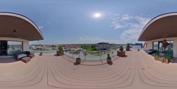 Terraço no telhado com assentos curvos, plantas em vasos e vista para a cidade.