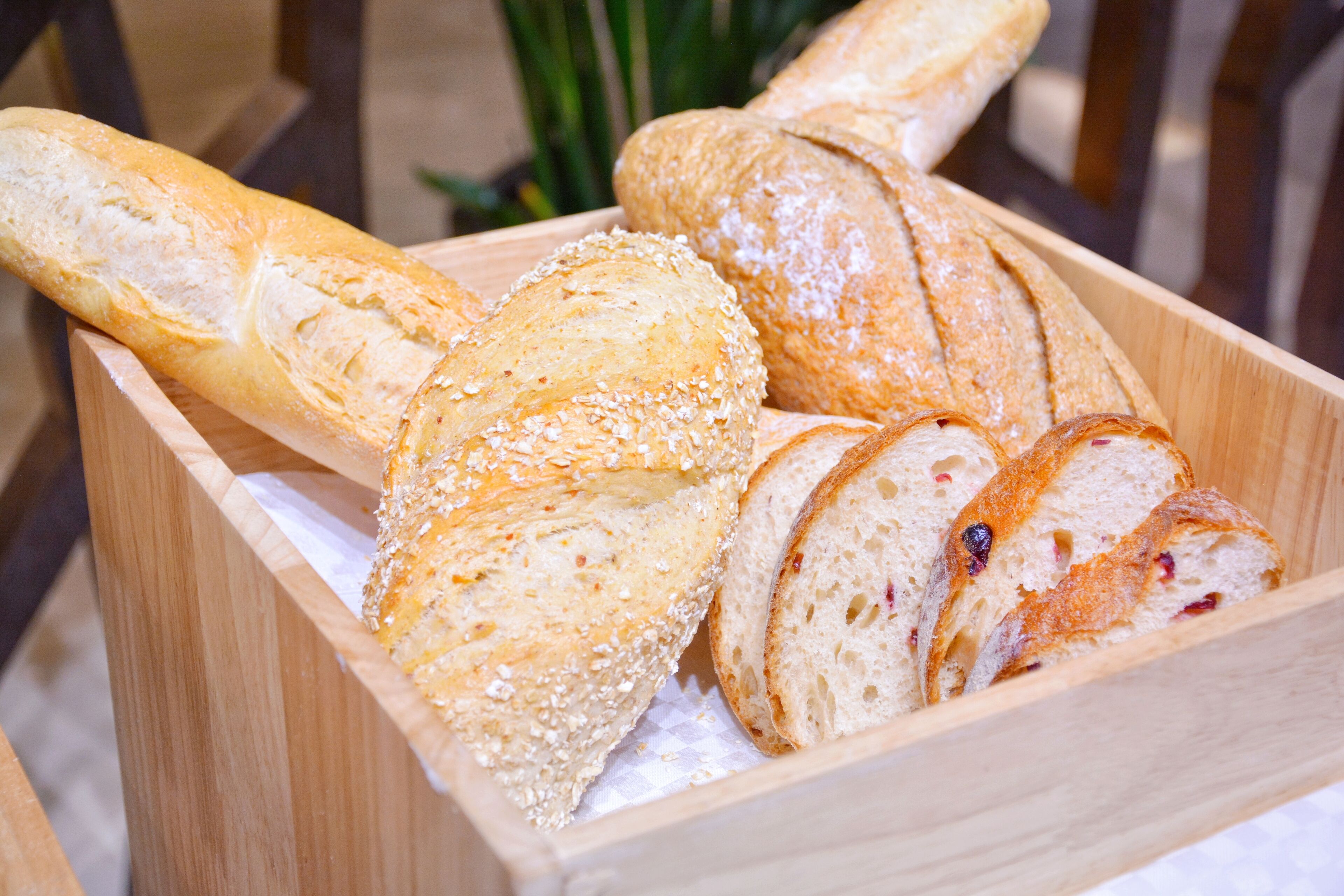 Uma caixa de madeira com vários tipos de pão, incluindo baguetes fatiadas e pães de enrolar.