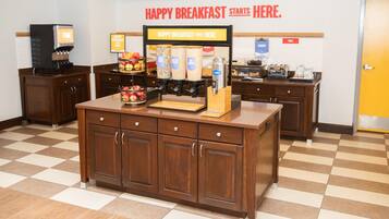 Um balcão de café da manhã com uma placa que diz 'HAPPY BREAKFAST STARTS HERE'. Há vários dispensadores de comida e uma saladeira no balcão.