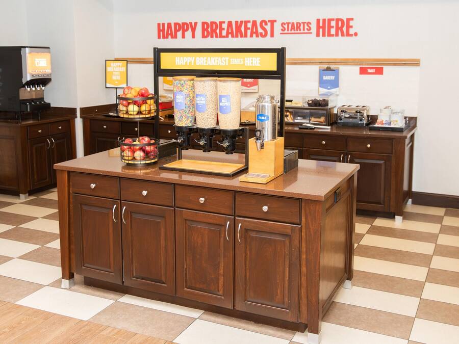 Um balcão de café da manhã com uma placa que diz 'HAPPY BREAKFAST STARTS HERE'. Há vários dispensadores de comida e uma saladeira no balcão.
