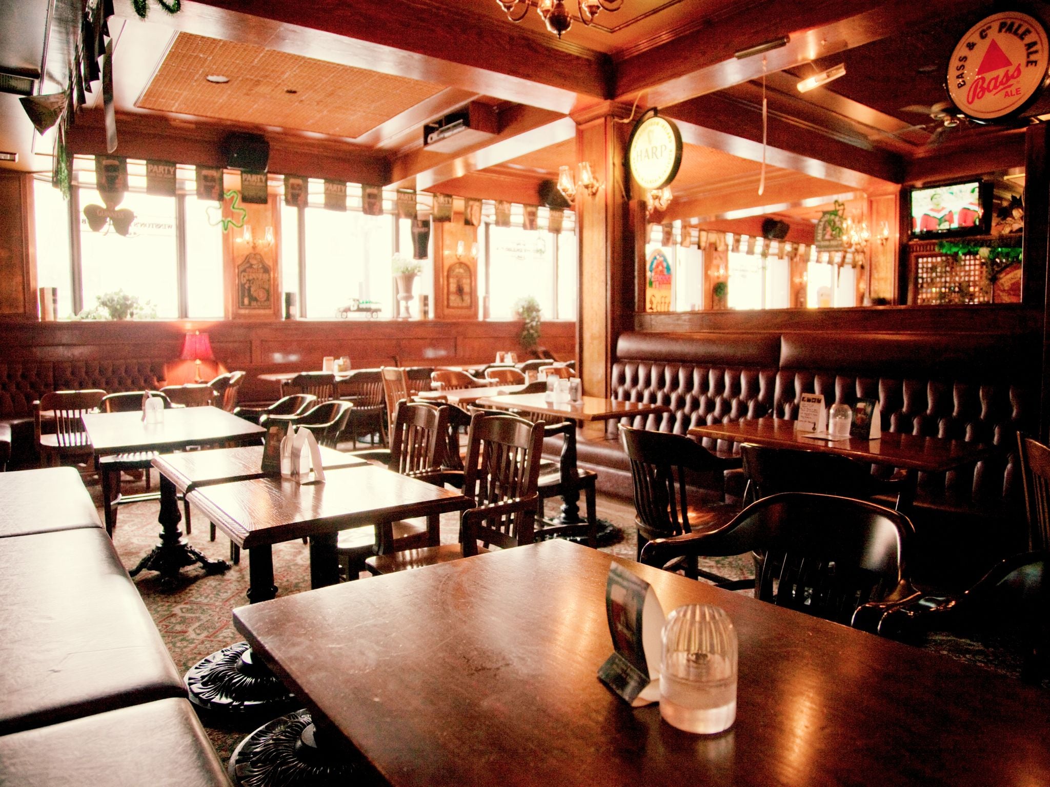 Interior de restaurante com mesas e bancos de madeira, área de bar e um relógio na parede.