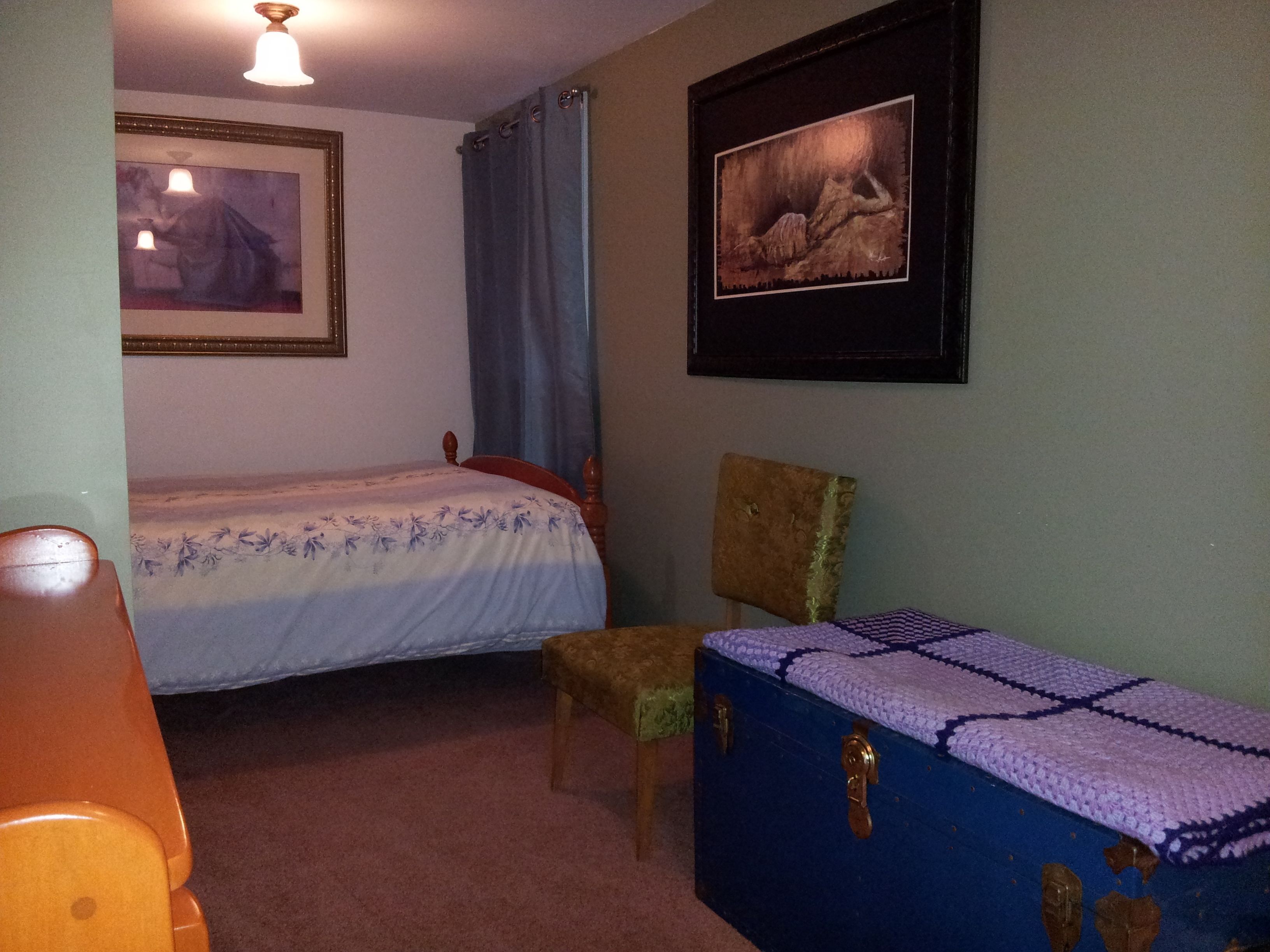 Quarto com cama, uma cadeira, cômoda e um quadro na parede.