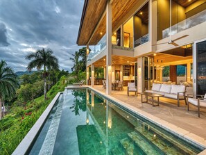 Uma casa moderna com uma piscina grande, área de estar ao ar livre e vista para o verde ao redor.