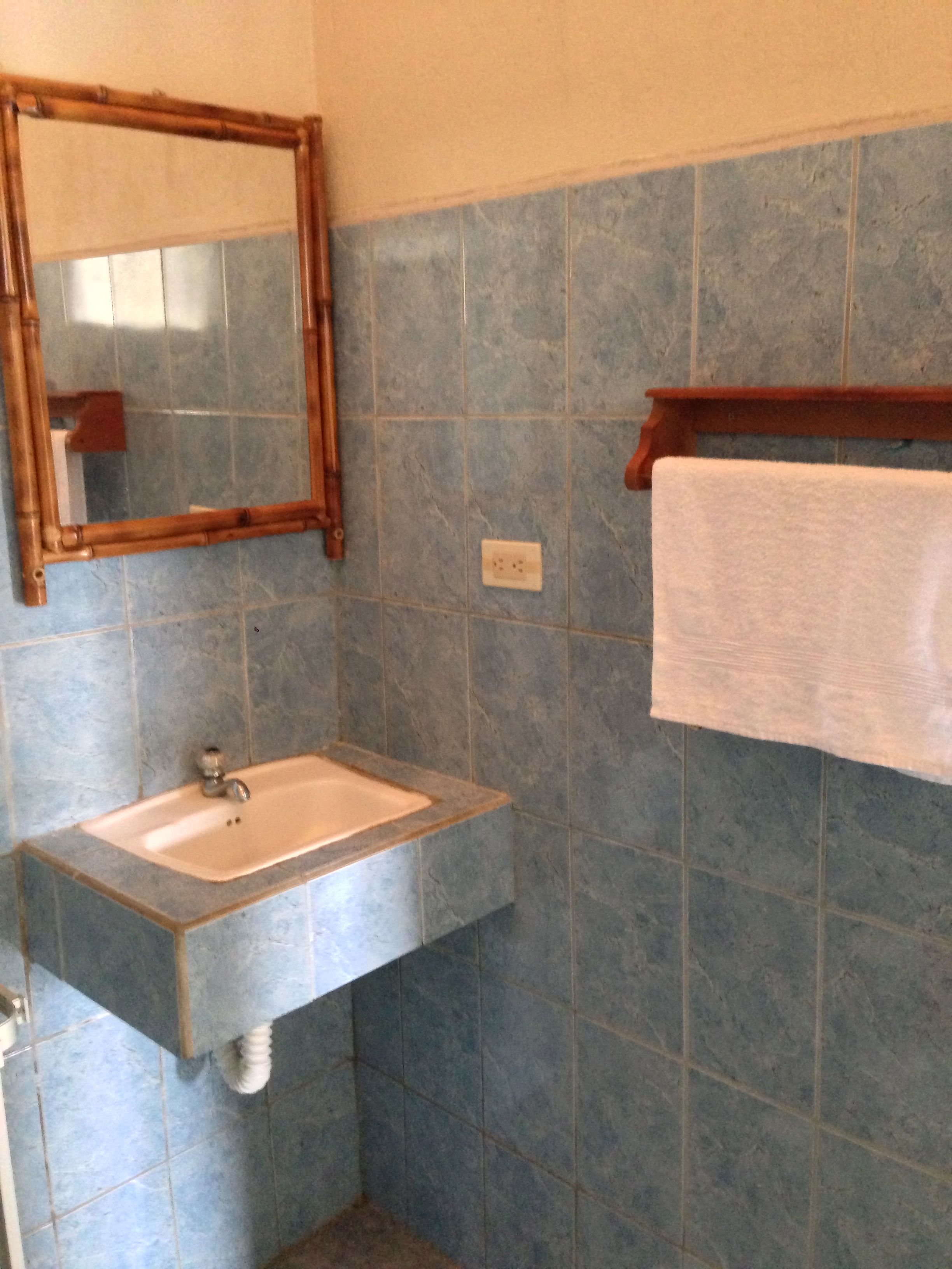 Casa de banho com uma sanita retangular, um espelho e um porta-toalhas.