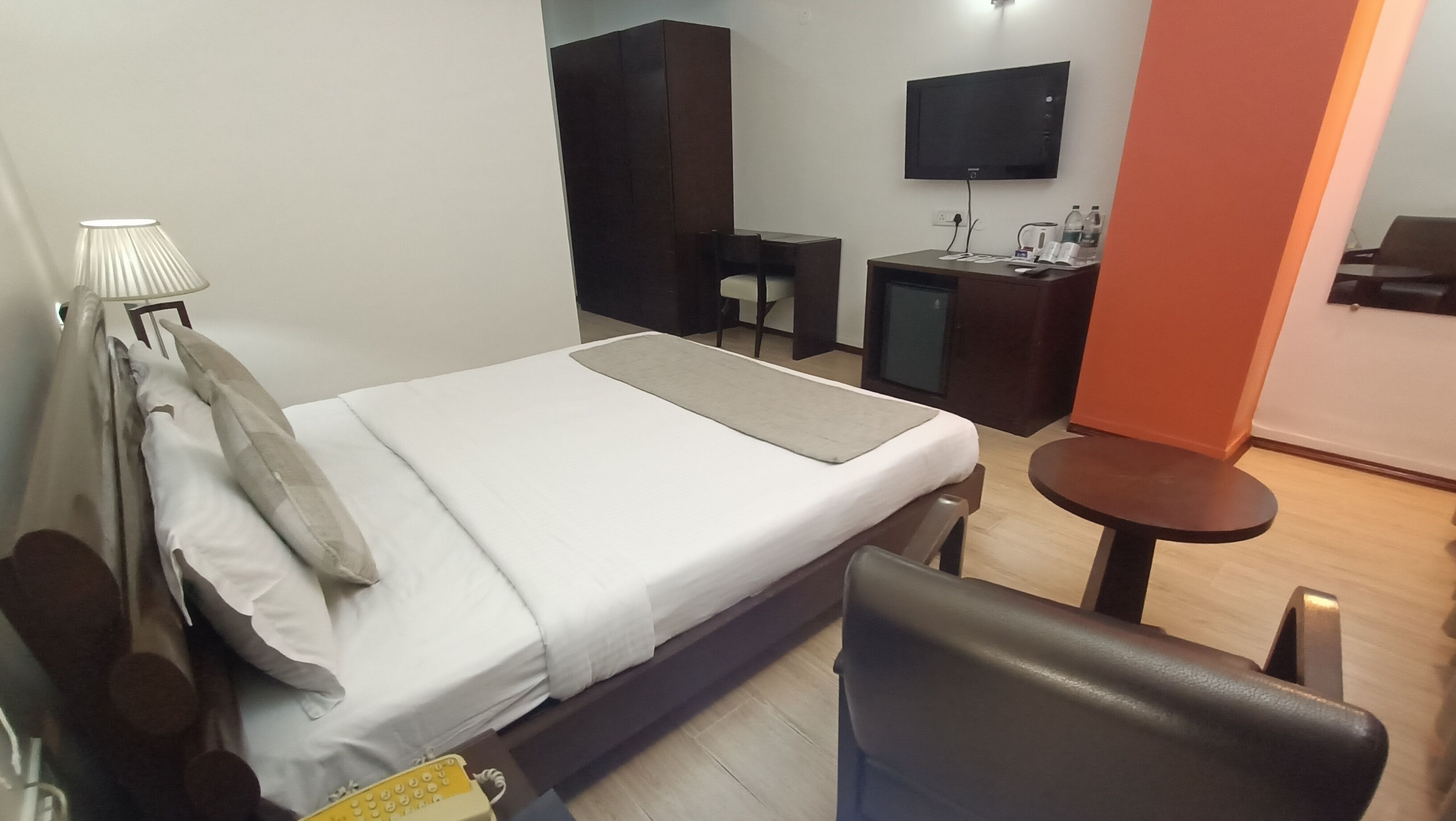 Quarto de hotel com cama, escrivaninha, cadeira, televisão e luminária.