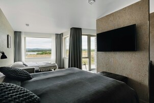 Quarto de hotel moderno com cama grande, TV de tela plana na parede e vista para o exterior.