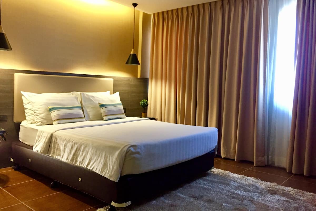 Quarto de hotel moderno com uma cama grande, mesa de cabeceira, luminária e vista para o exterior através das cortinas.