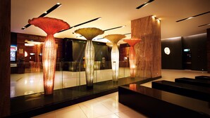 Um lobby moderno com guarda-corpo de vidro, balcão de recepção e uma grande escultura em vaso.