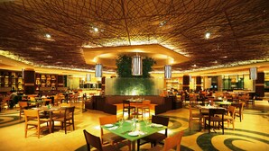 Um restaurante espaçoso com várias mesas e cadeiras, uma planta decorativa no centro e piso estampado.
