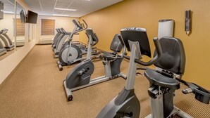 Uma academia com bicicletas ergométricas, esteiras e um espelho grande na parede.