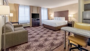 Quarto de hotel com cama, escrivaninha, cadeira, televisão e frigorífico.