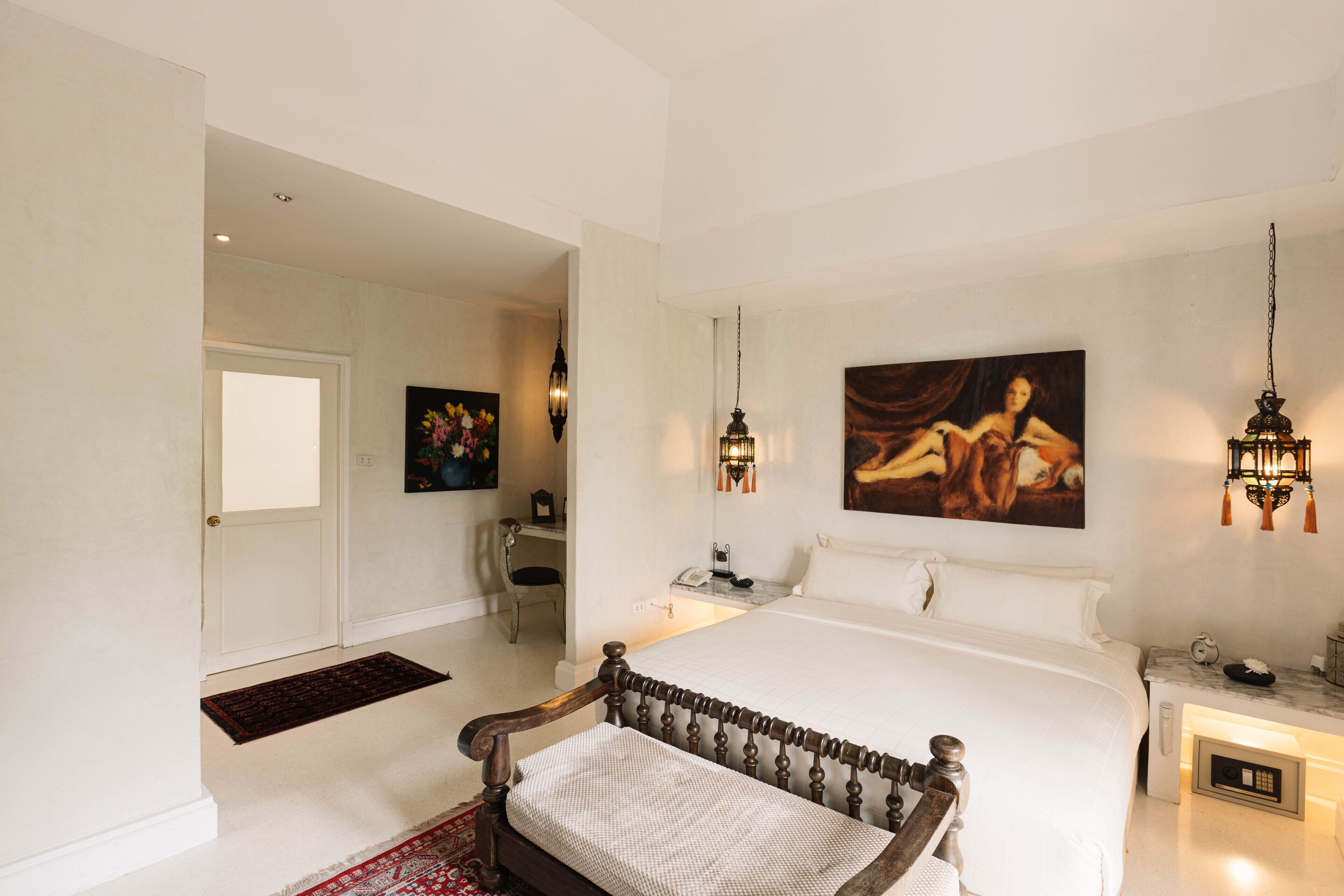 Quarto com cama grande, mesa de cabeceira, escrivaninha, cadeira e um quadro na parede.