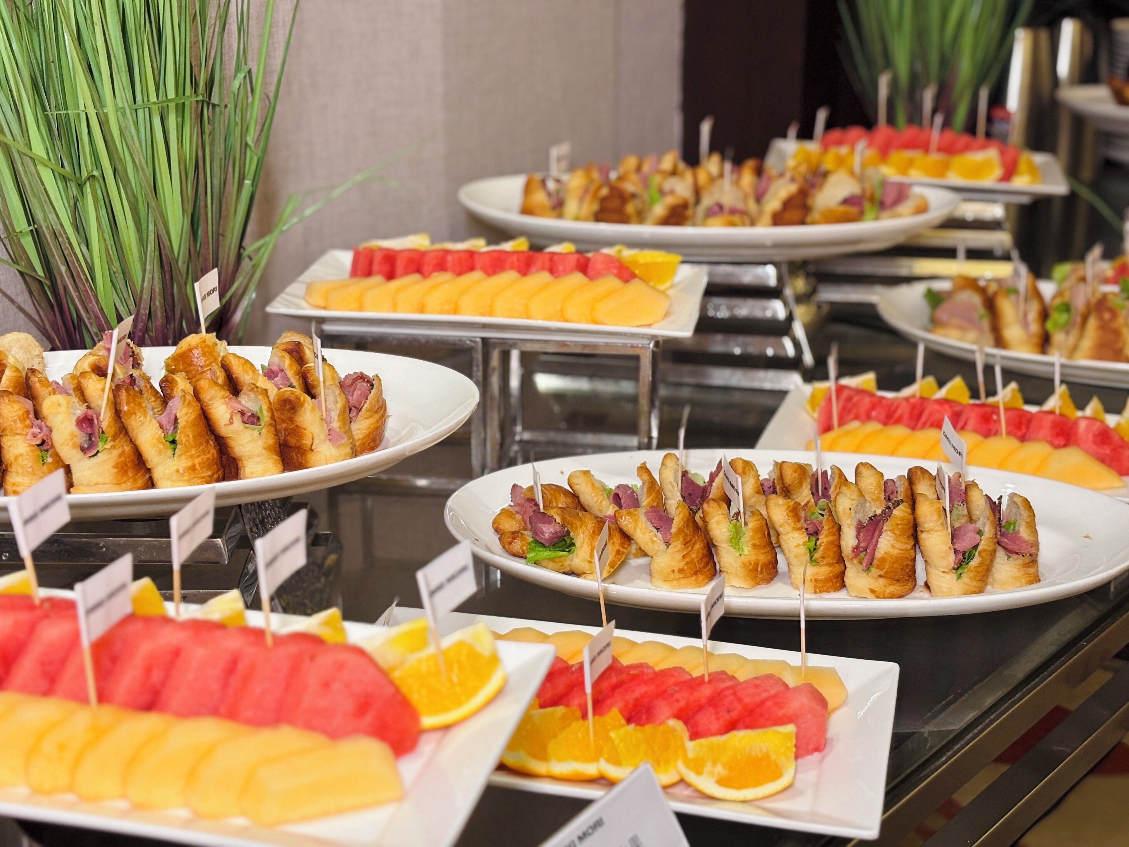 Buffet com diversos itens de comida, incluindo croissants, frutas e sanduíches.