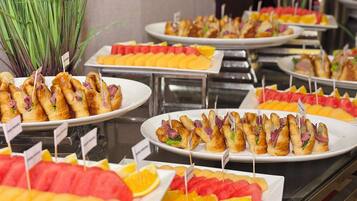 Buffet com diversos itens de comida, incluindo croissants, frutas e sanduíches.