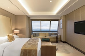 Quarto de hotel com uma cama grande, um sofá, uma TV e vista para o mar.