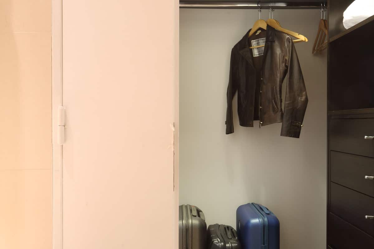 Um closet espaçoso com uma jaqueta de couro pendurada, duas malas e piso de madeira.