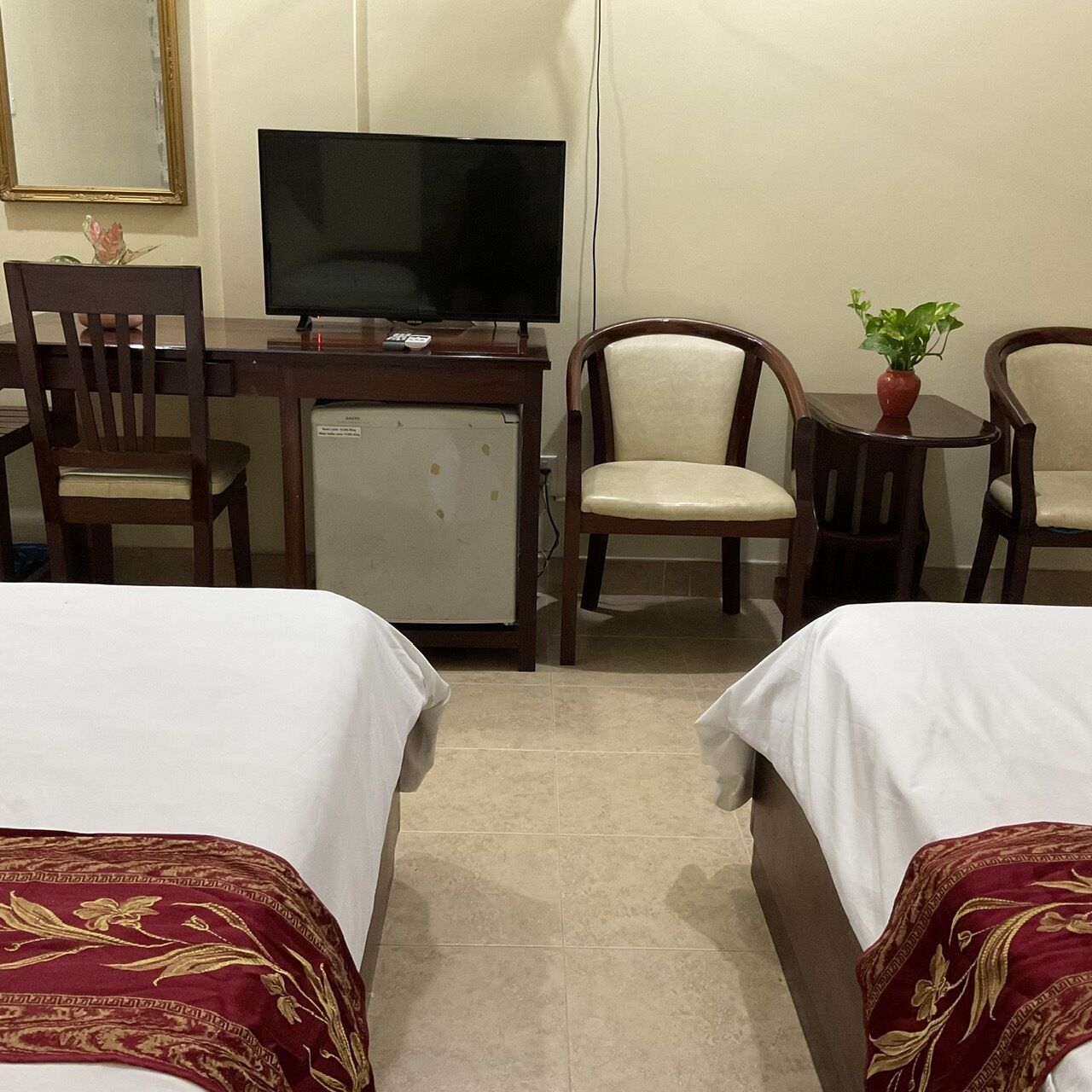 Quarto de hotel com duas camas, uma mesa de trabalho com televisão, um frigorífico pequeno e duas cadeiras.