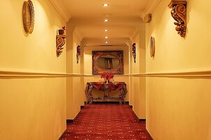 Um corredor com tapete vermelho, decoração de parede ornamentada e um espelho no final.