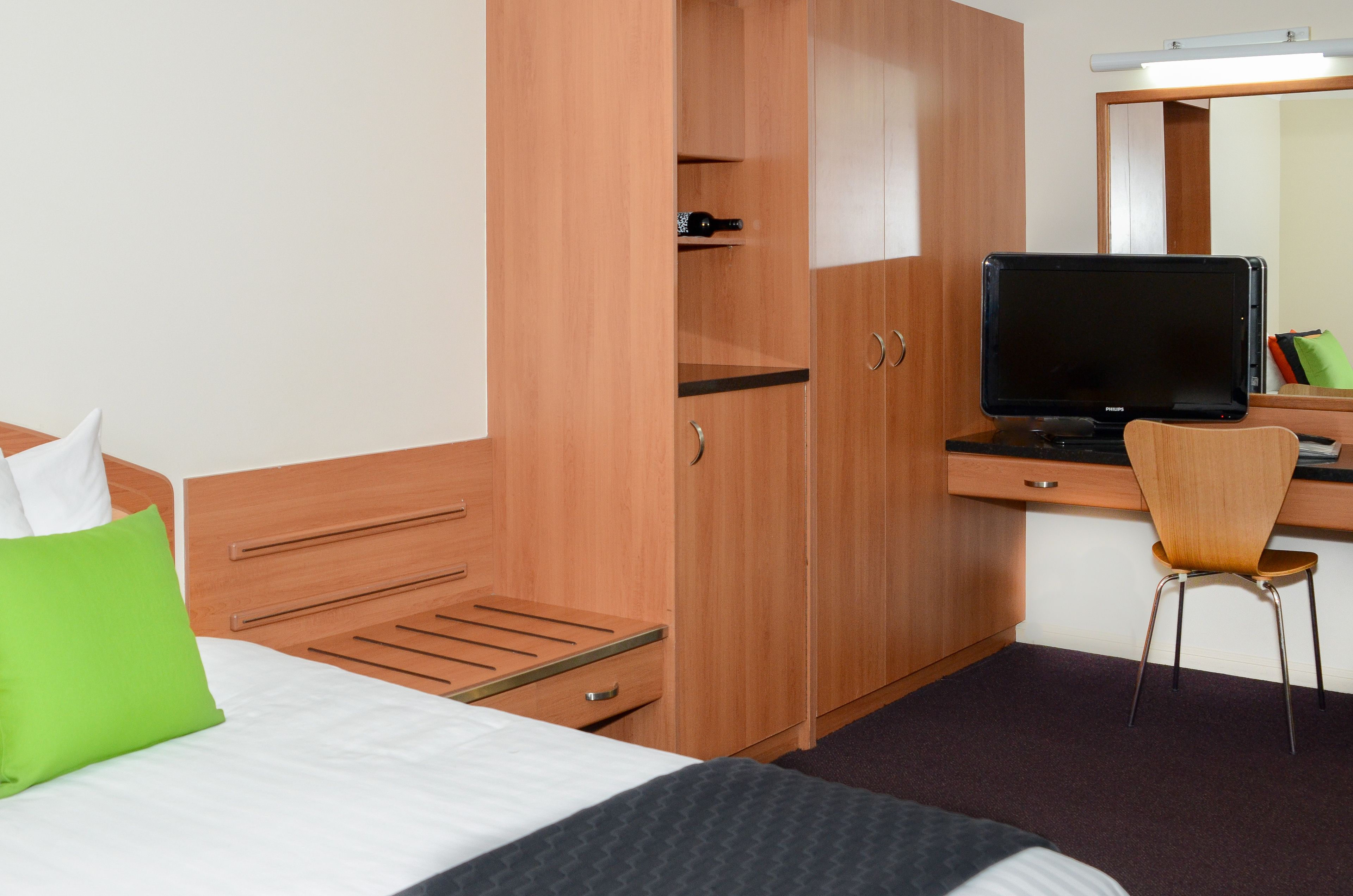 Quarto de hotel com cama, secretária com computador, cadeira, guarda-roupa e espelho.