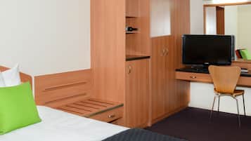 Quarto de hotel com cama, secretária com computador, cadeira, guarda-roupa e espelho.
