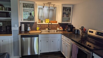 Uma cozinha moderna com armários brancos, lava-louças de aço inoxidável, uma pia dupla e bancada preta.