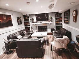 Uma sala de estar moderna com sofás de couro, lareira, estantes e uma TV na parede.
