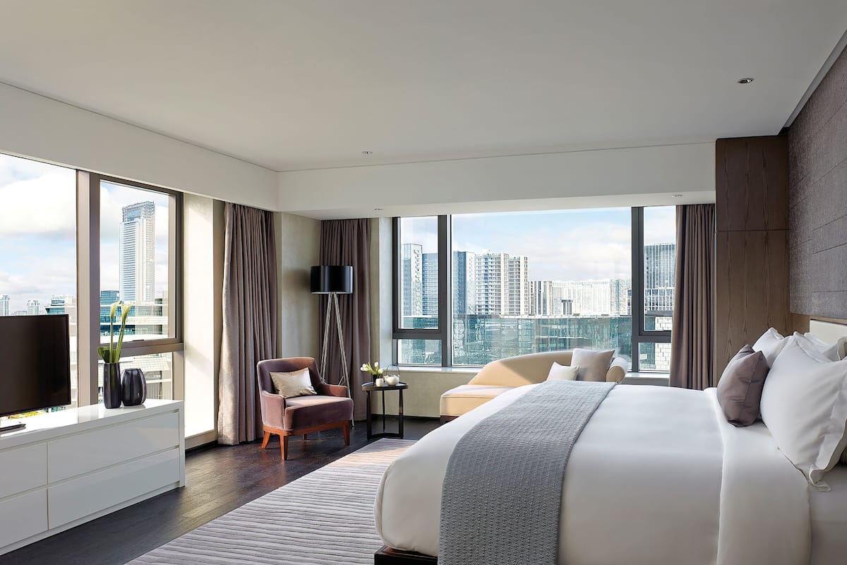 Quarto de hotel moderno com uma cama grande, área de estar e vista para a cidade.