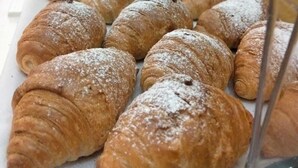 Uma bandeja com diversos doces e pães, incluindo croissants e outros produtos de pastelaria, exposta sobre uma mesa.