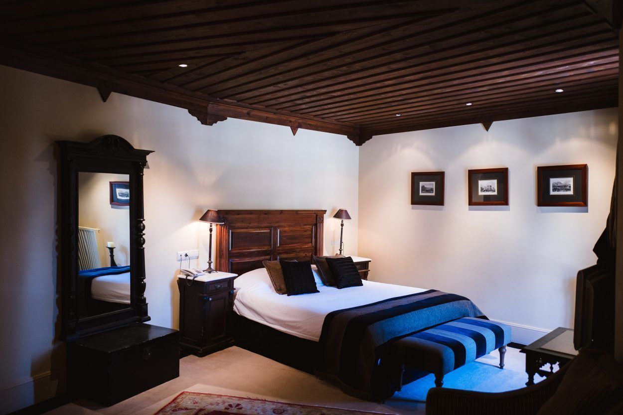Quarto com cabeceira de madeira, um espelho grande, mesas de cabeceira, cama com manta listrada e quadros nas paredes.