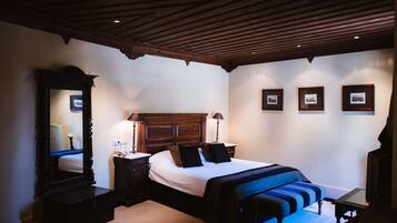 Quarto com cabeceira de madeira, um espelho grande, mesas de cabeceira, cama com manta listrada e quadros nas paredes.