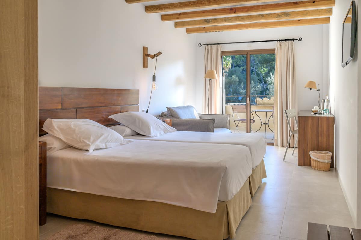 Quarto com duas camas, cabeceira de madeira, janela com cortinas, escrivaninha e uma cadeira.