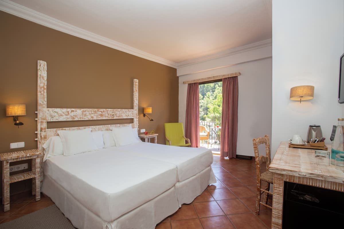 Quarto de hotel com uma cama grande, duas mesas de cabeceira, uma cadeira, escrivaninha com abajur e vista para o exterior.