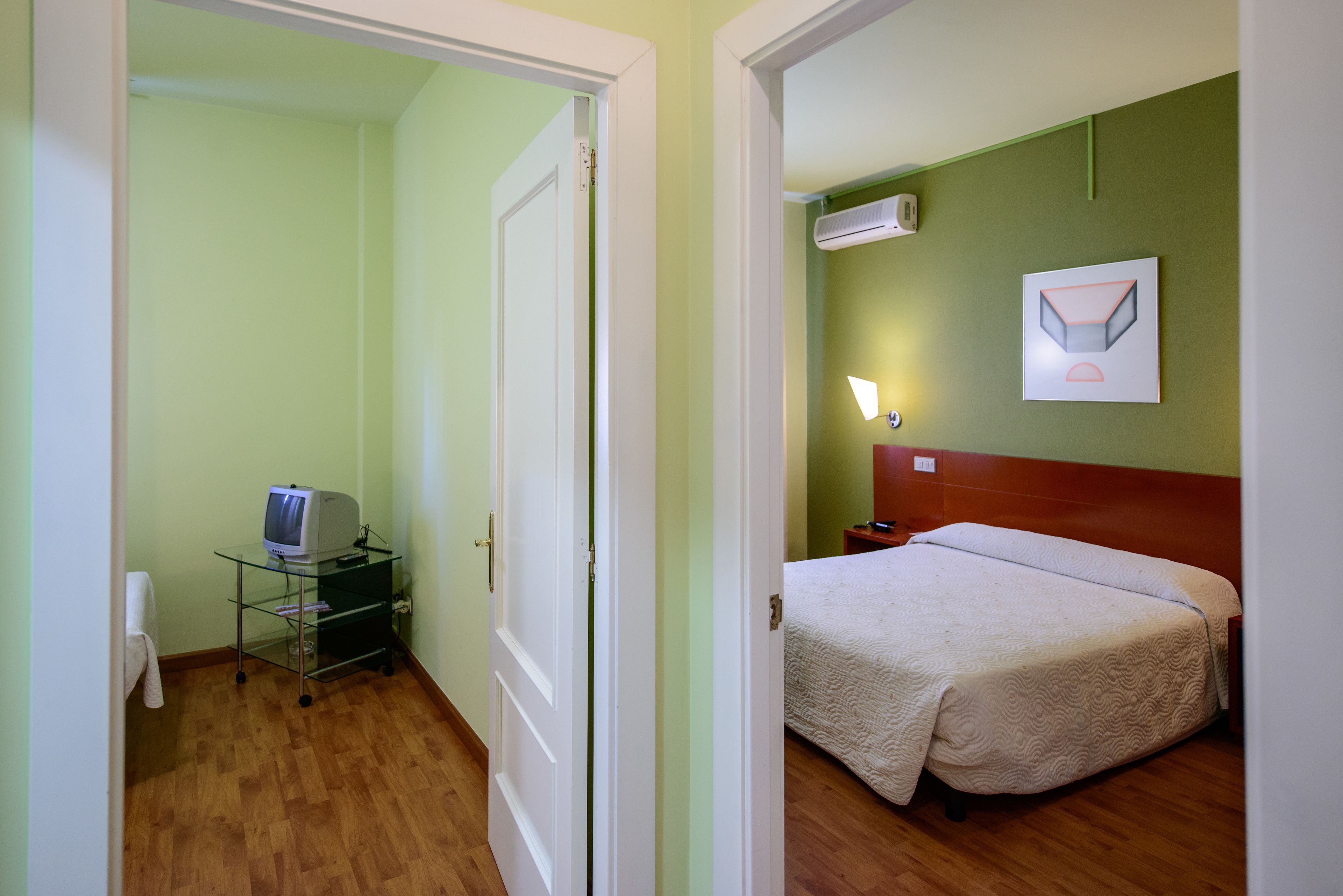 Quarto de hotel com uma cama, uma televisão sobre uma mesa de vidro e um ar condicionado fixado na parede.