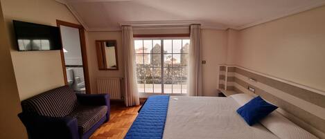 Quarto de hotel com cama, sofá, televisão, janela com cortinas e vista para prédios.