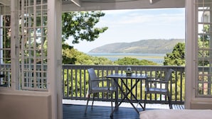 Varanda com mesa e cadeiras, com vista panorâmica para um lago e colinas.