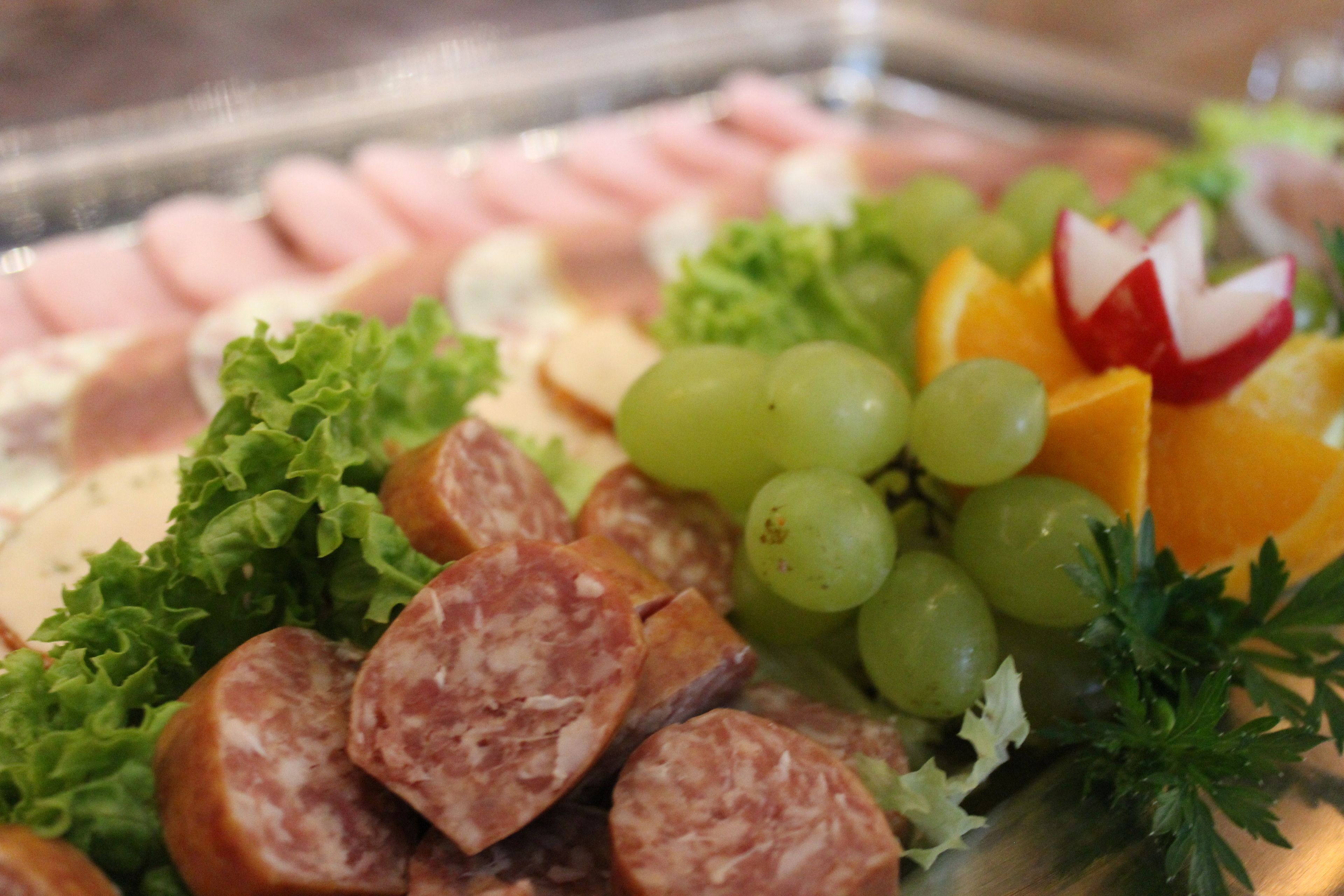 Uma travessa com fatias de carne, uvas e frutas cítricas.