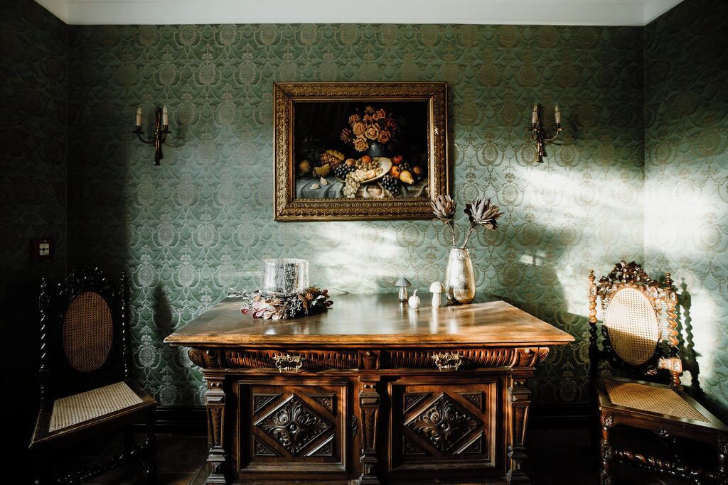 Uma sala de jantar com mesa de madeira, cadeiras, um quadro emoldurado e arandelas na parede.