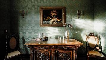 Uma sala de jantar com mesa de madeira, cadeiras, um quadro emoldurado e arandelas na parede.
