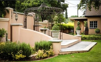 Um jardim ajardinado com um gazebo, uma parede curva e um caminho que leva a um edifício.