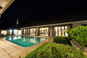 Piscina com área de pátio, espaço de estar coberto ao ar livre e paisagismo bem cuidado.