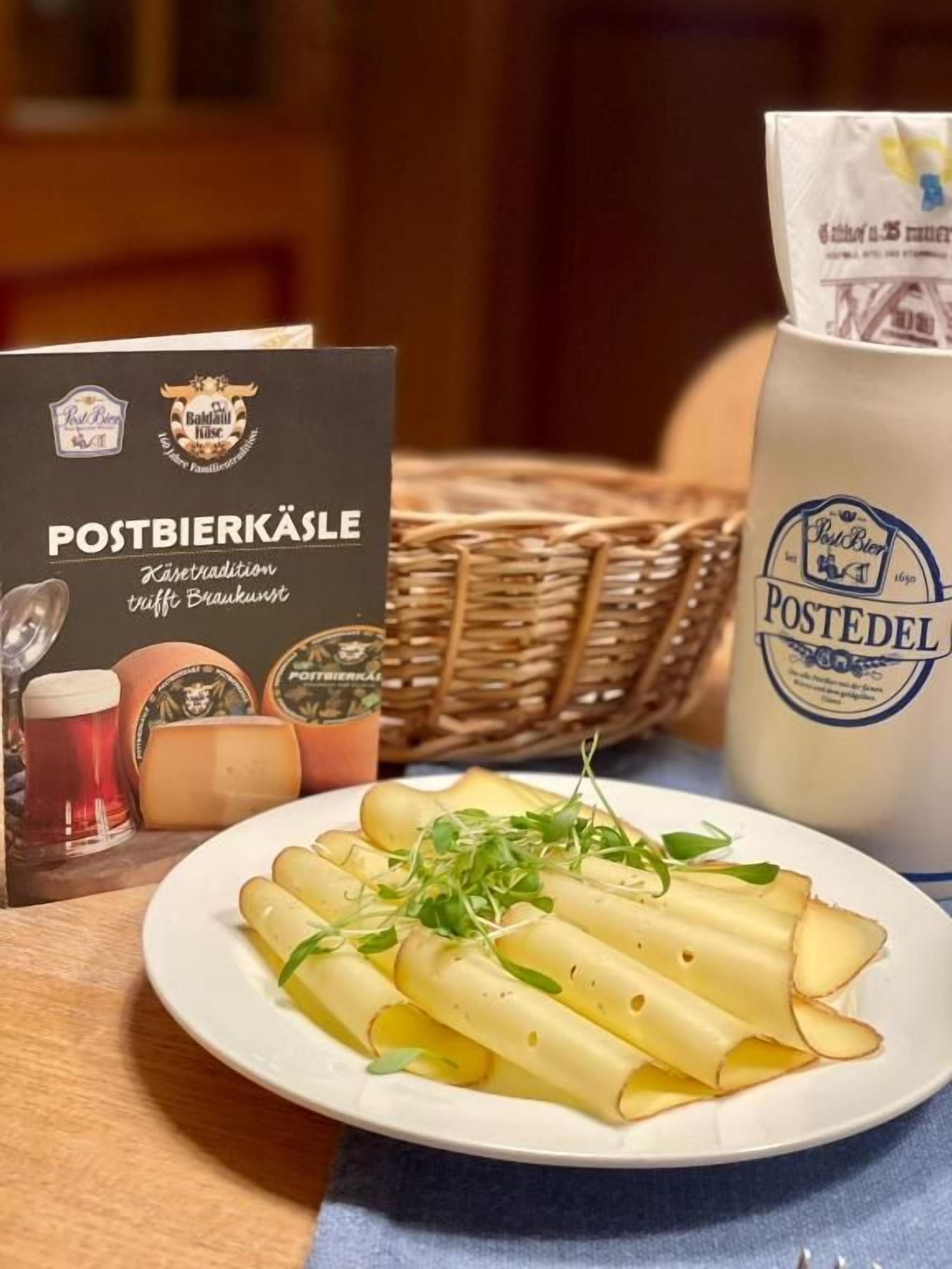 Um prato de panquecas enroladas com a etiqueta 'POSTBIERKÄSLE' e uma garrafa de cerveja 'POSTEDEL'.