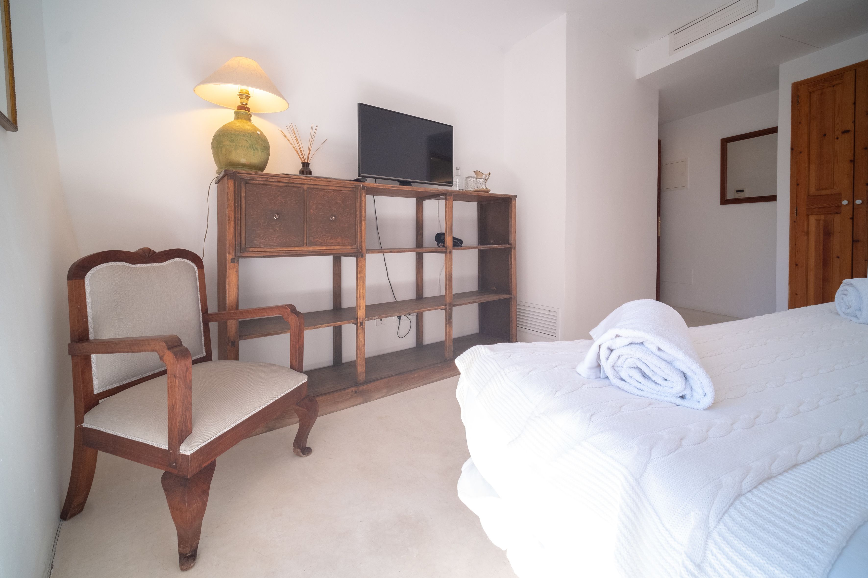 Um quarto com uma cama, uma escrivaninha de madeira com uma televisão, uma cadeira e um abajur.