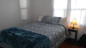 Quarto com uma cama, luminária de cabeceira e janela com persianas.