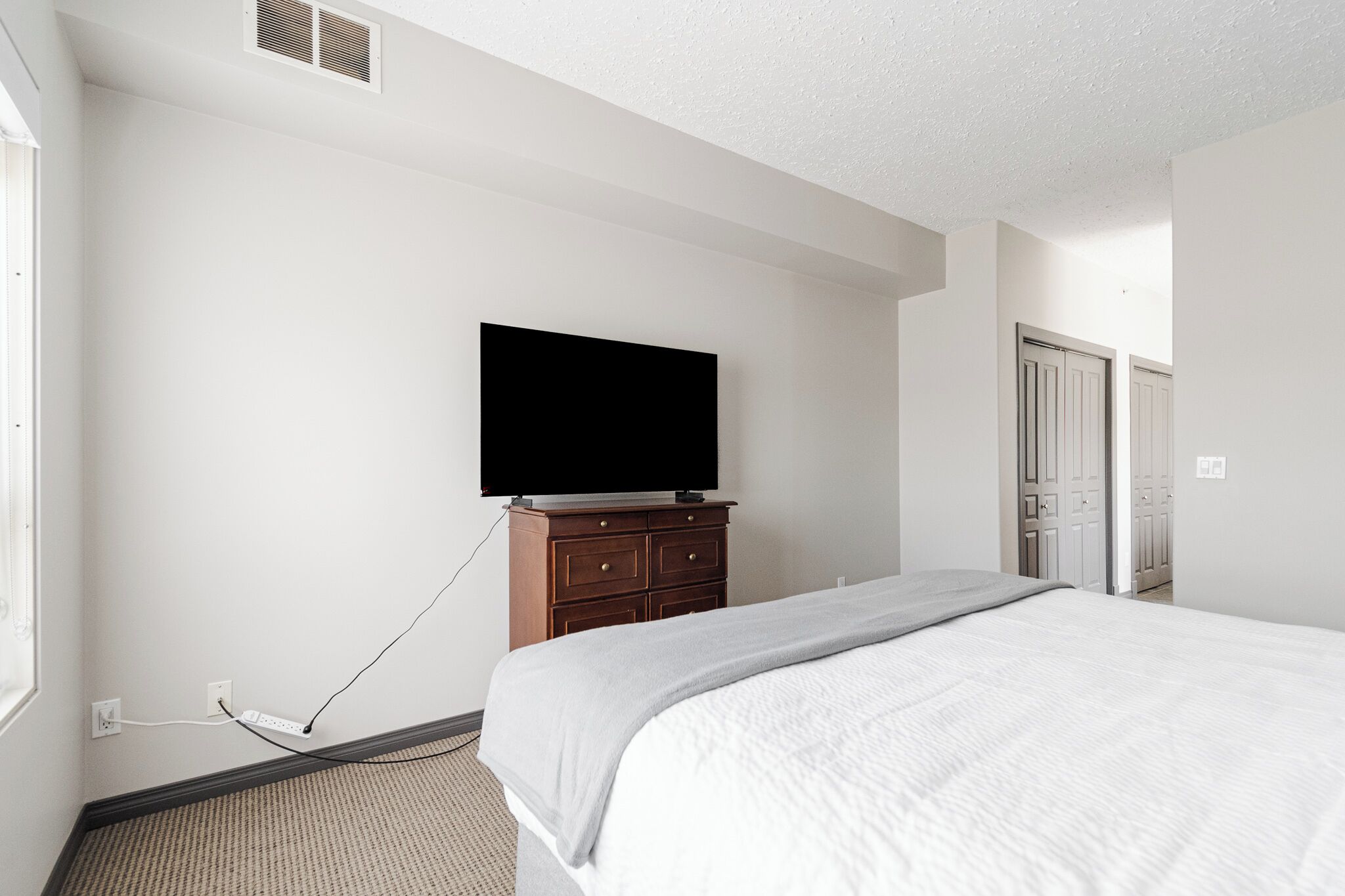 Quarto de hotel com cama, cômoda, televisão fixada na parede e porta à direita.