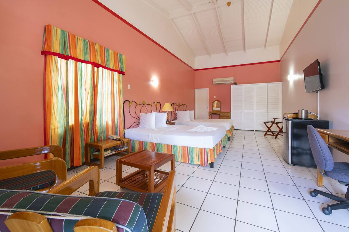 Quarto de hotel com cama, escrivaninha, cadeira, televisão e janela com cortinas.